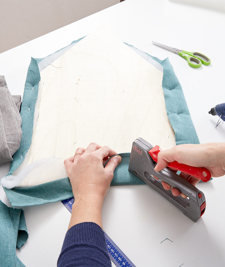 Mit einem Tacker wird das Vlies und der Stoff am Sperrholz befestigt ...